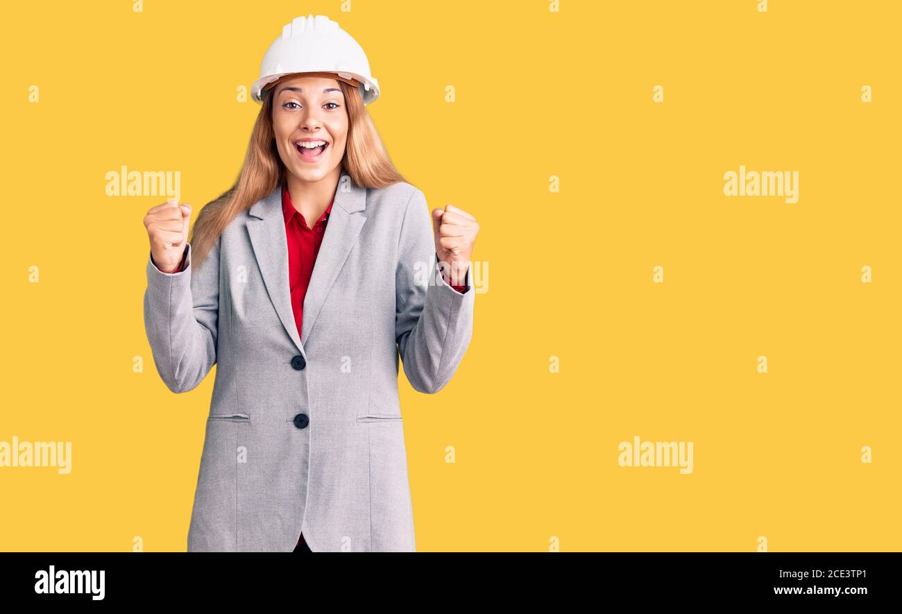 Schöne junge Frau trägt Architekt Hardhut feiert überrascht und ... Schöne junge Frau trägt Architekt Hardhut feiert überrascht und ...