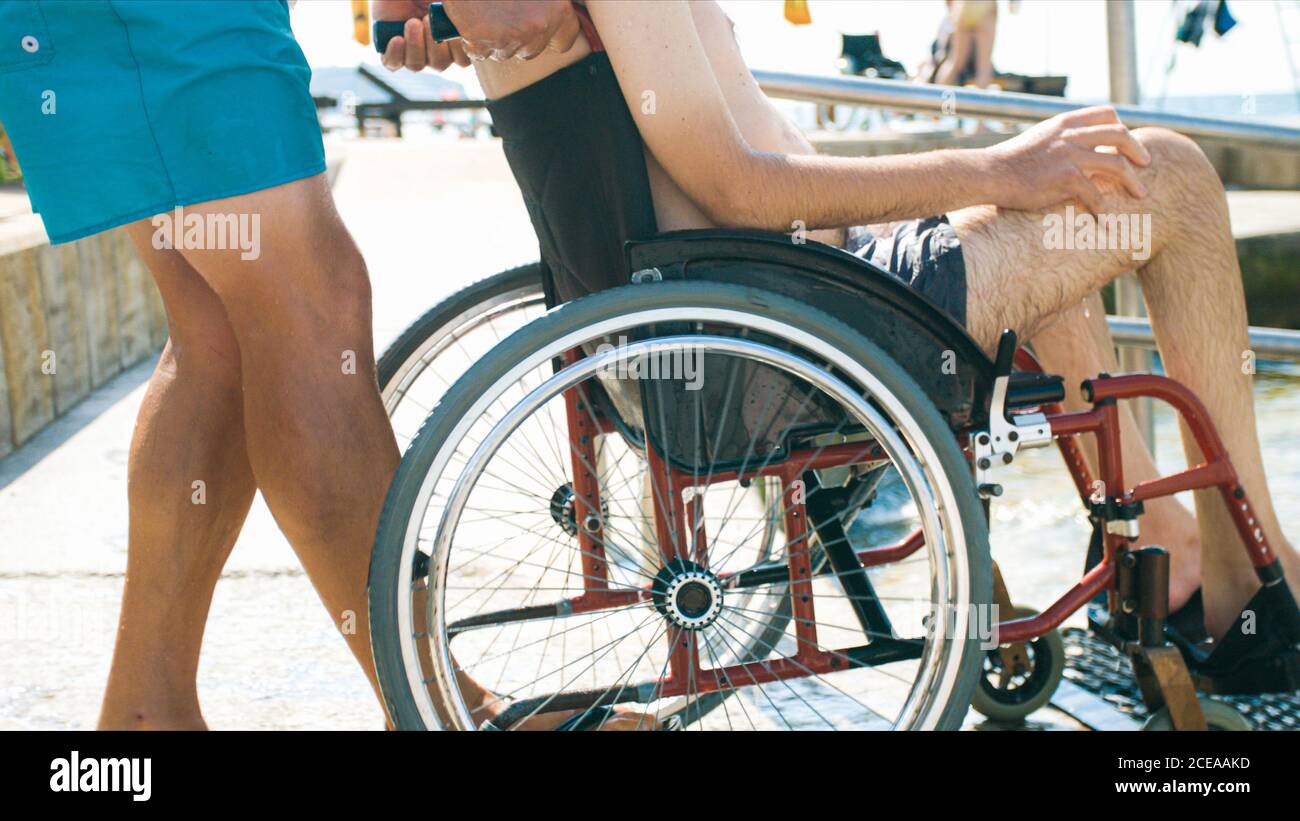Behinderter Mann am Strand schwimmt auf einem Rollstuhl mit Hilfe auf ...