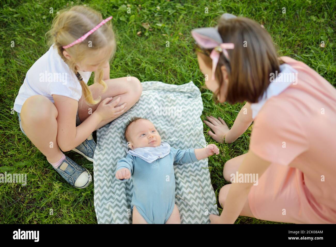 Zwei große Schwestern bewundern ihren liebenswerten kleinen Bruder. Zwei junge Mädchen mit ihrem ...