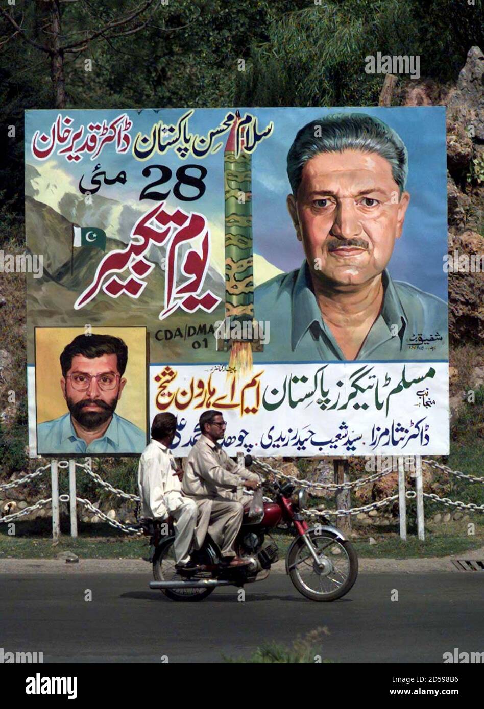 Zwei Pakistaner auf einem Motorrad pass ein Plakat mit einem Porträt ...