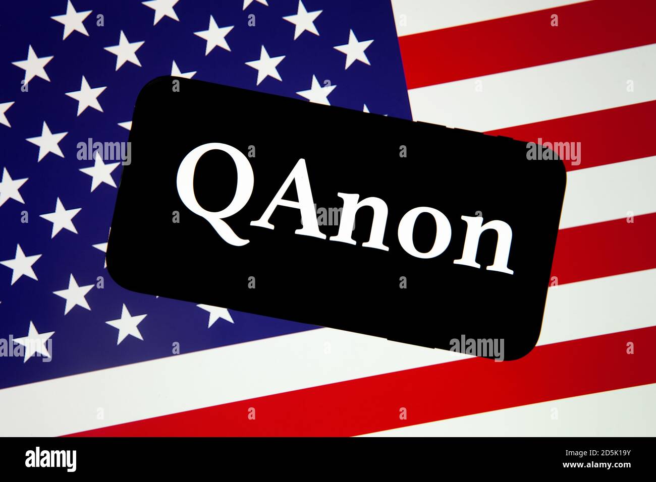 QAnon-Logo auf dem Smartphone, das auf der USA-Flagge platziert ist. Konzept für QAnon oder Q ...