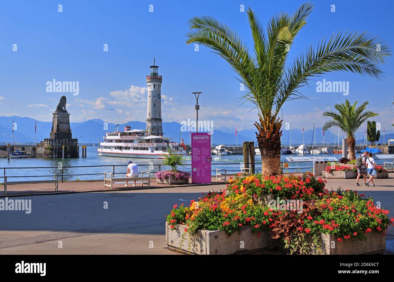Blumenkästen und Palmen an der Hafenpromenade und Ausflugsboot in der ...