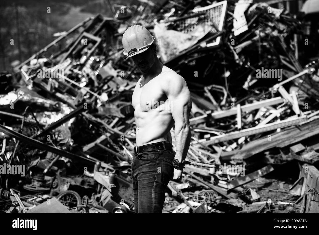 Junger Mann steht stark in Old Scrap Metal Garage und Flexing Muscles ...