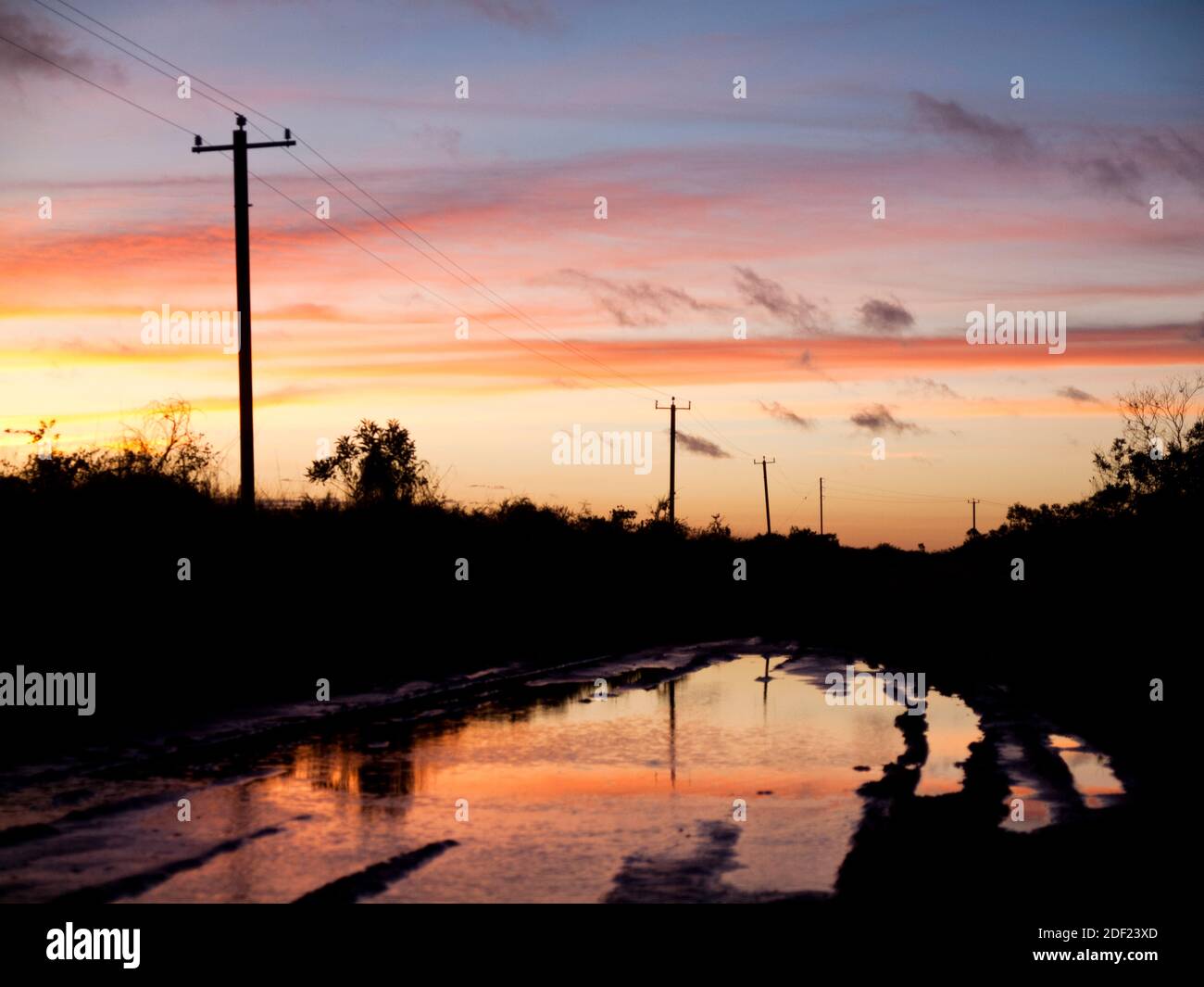 Sonnenuntergang in einer Pfütze mit Telegrafenmasten entlang der Kavite ...