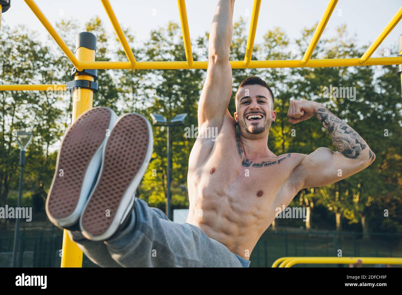Lustiger sportlicher junger Mann, der an den Bars hängt und seine zeigt ...