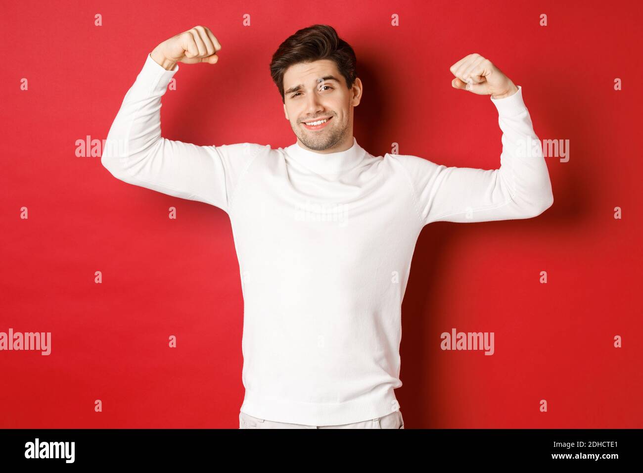 Portrait von lächelnd schöner Mann in weißem Pullover, Biegen Bizeps ...