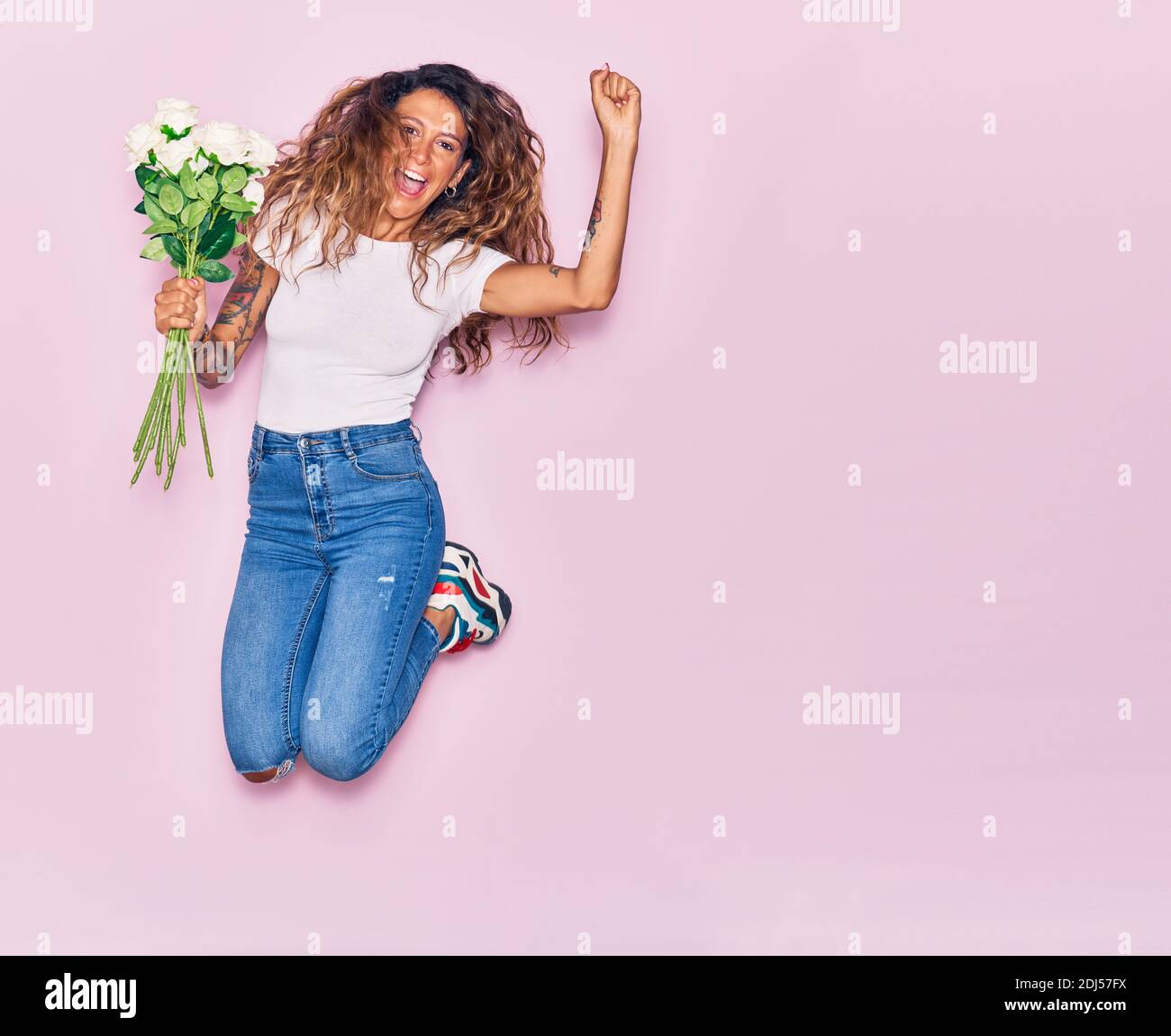 Junge schöne lockige Frau mit Tattoo halten Strauß von weißen Rose ...