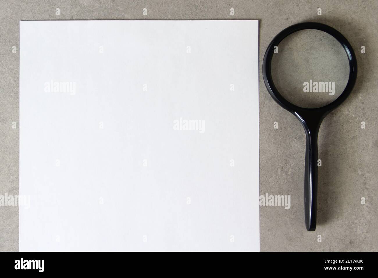 Vorlage aus weißem Papier mit einer Lupe auf hellgrauem Betongrund ...