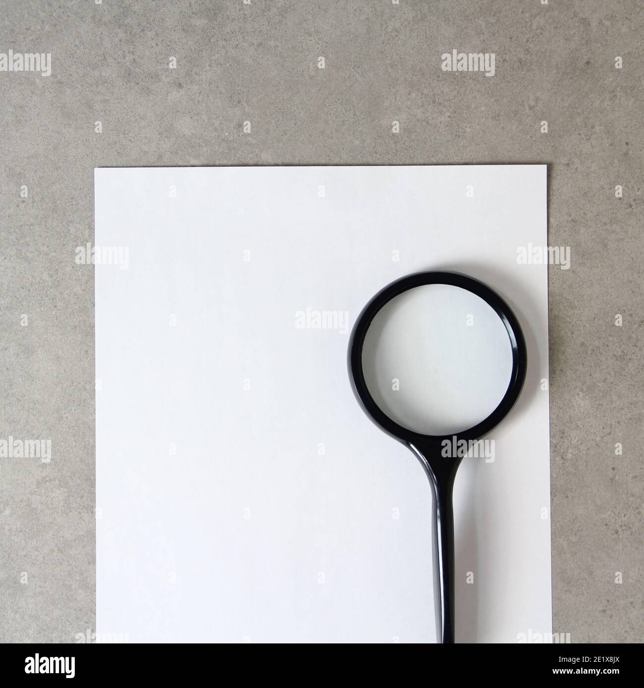 Vorlage aus weißem Papier mit einer Lupe auf hellgrauem Betongrund ...