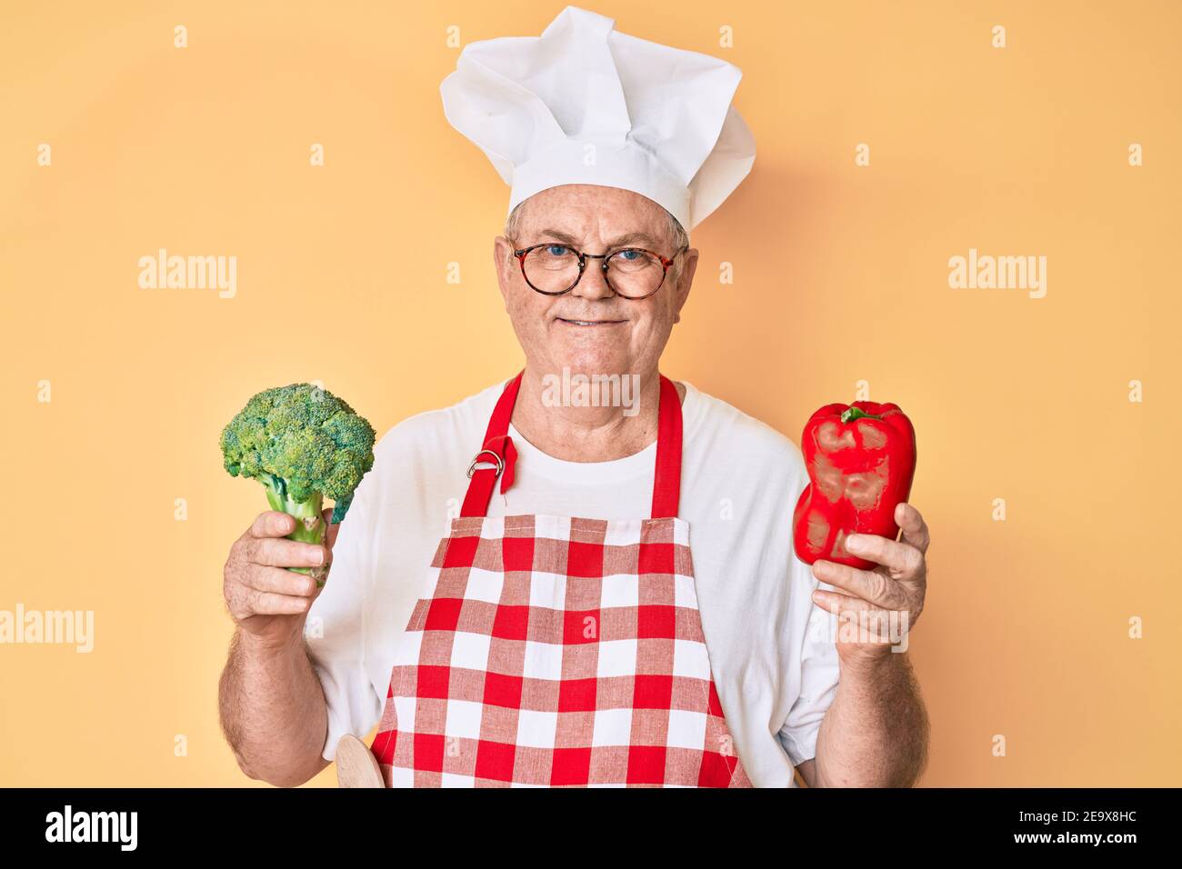 Senior grauhaarige Mann trägt professionelle Koch Schürze hält Brokkoli ...