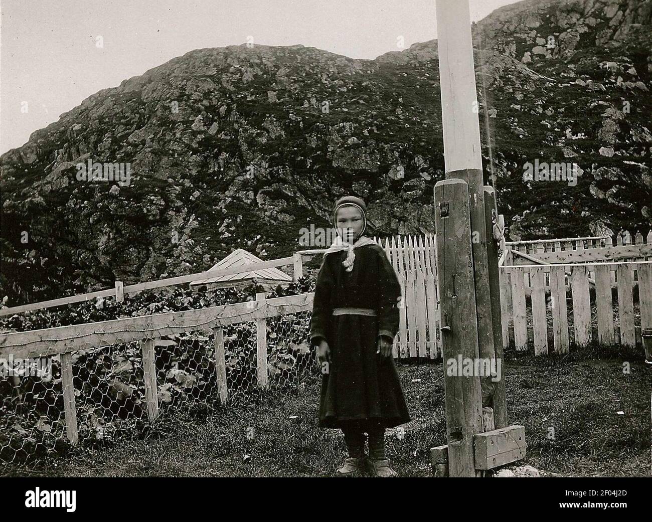 Hecht i samisk drakt stående ved flaggstang foran innngjerdet ...