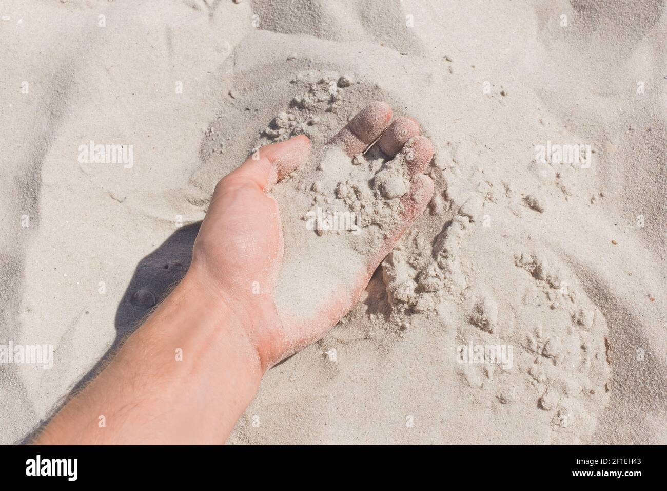 Die Hand des Typen nimmt oder berührt den weißen Strandsand aus ...
