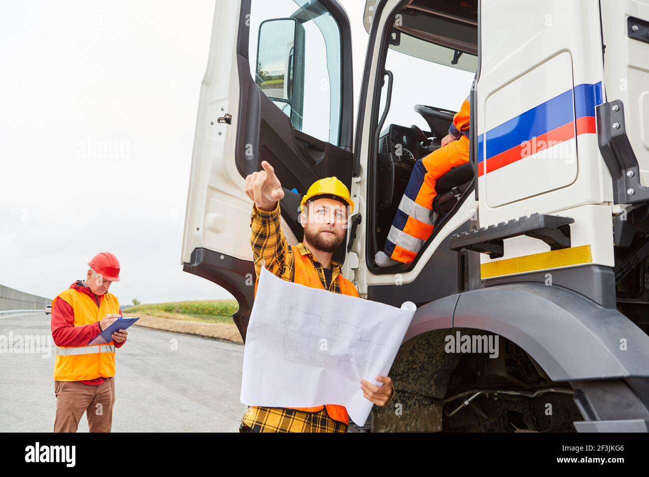 Bauarbeiter als Vorarbeiter im Straßenbau geben LKW-Fahrer Anweisungen ...