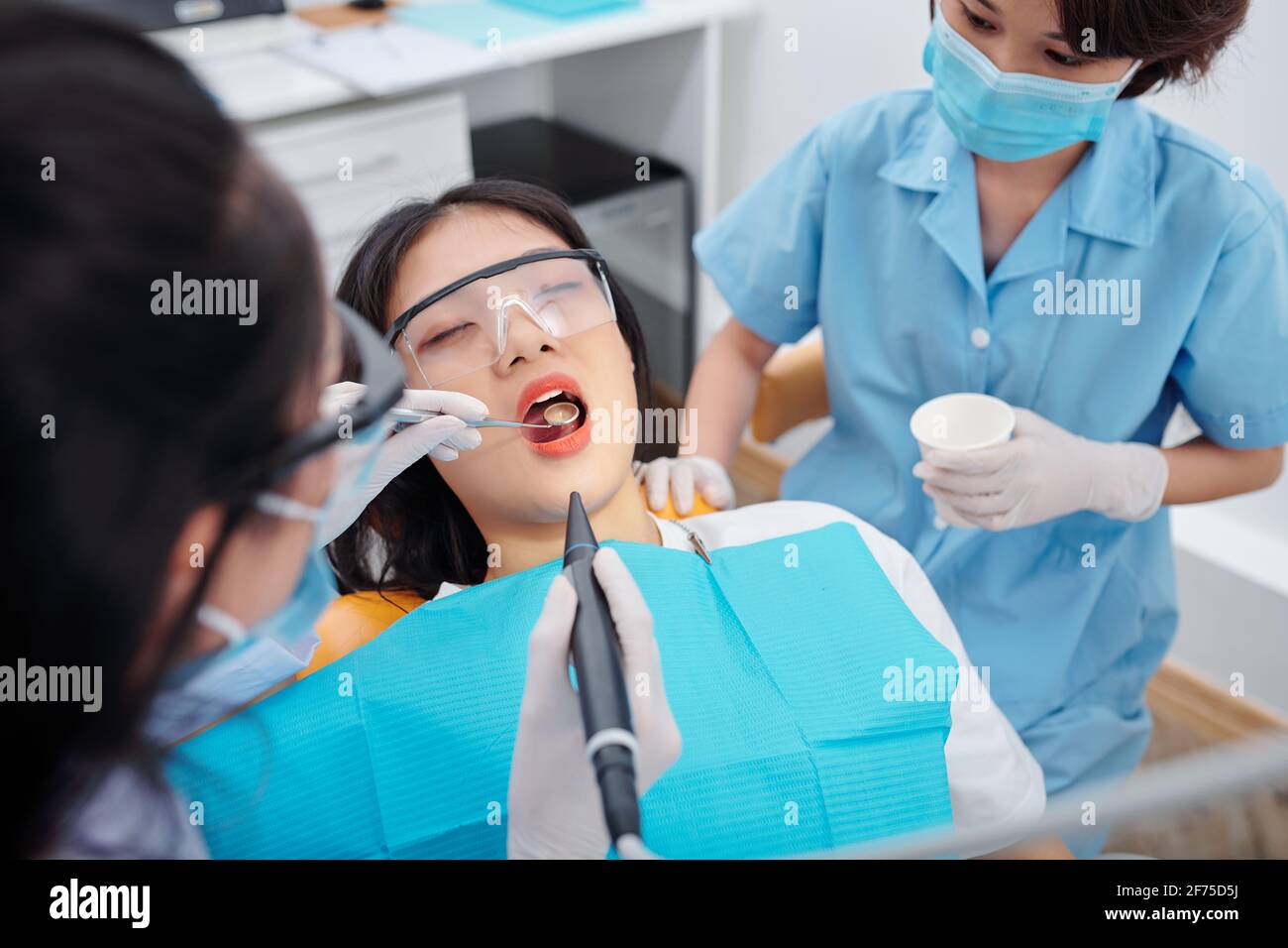 Zahnarzt, der Zähne von jungen weiblichen Patienten bohrt, die an Zahnschmerzen leiden ...