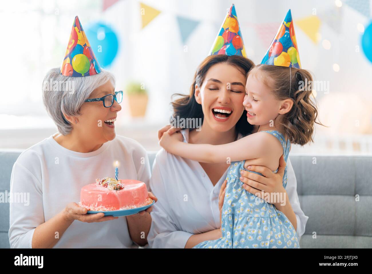Das Kind bläst die Kerzen auf dem Kuchen aus. Großmutter, Mutter und Tochter feiern Geburtstag ...