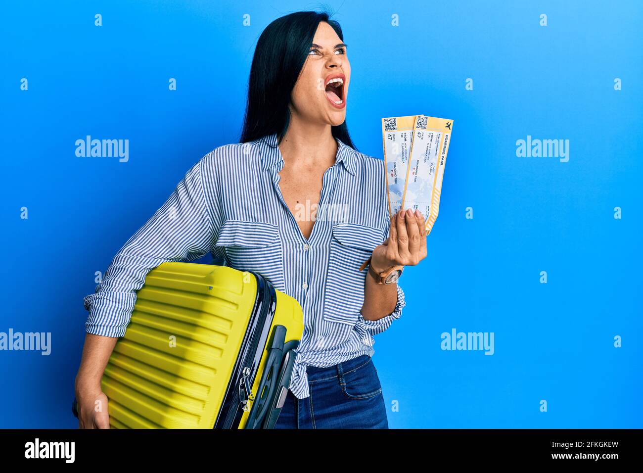 Junge kaukasische Frau mit Hüttenkoffer und Bordkarten wütend und ...