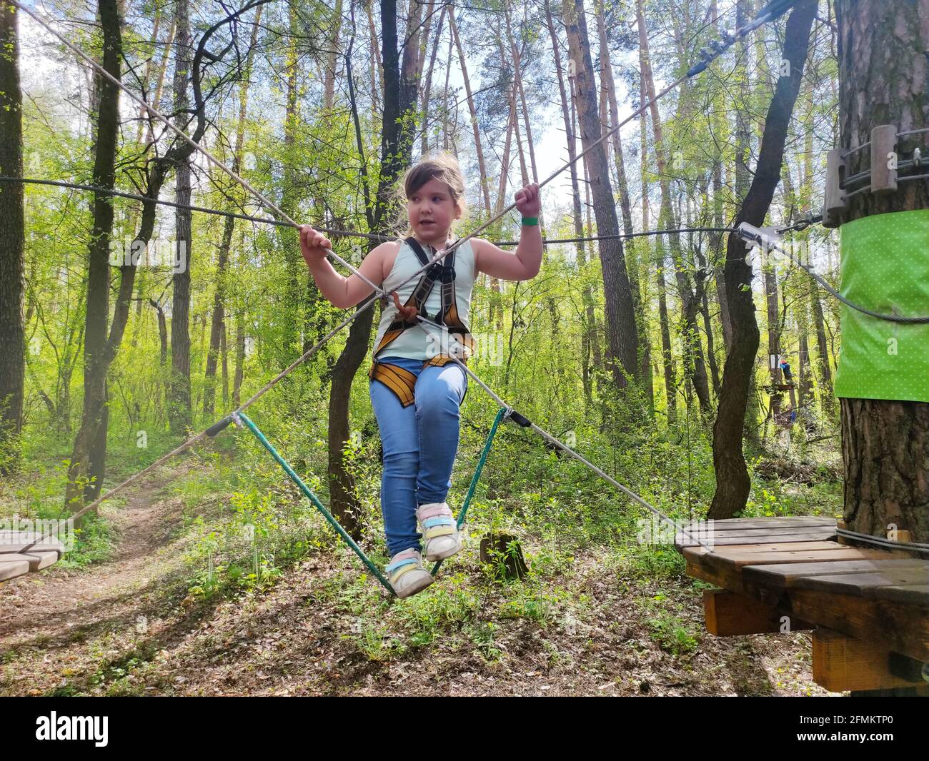Kleine kaukasische blonde Mädchen spielt im Park oder Wald, Seilpark im ... Kleine kaukasische blonde Mädchen spielt im Park oder Wald, Seilpark im ...