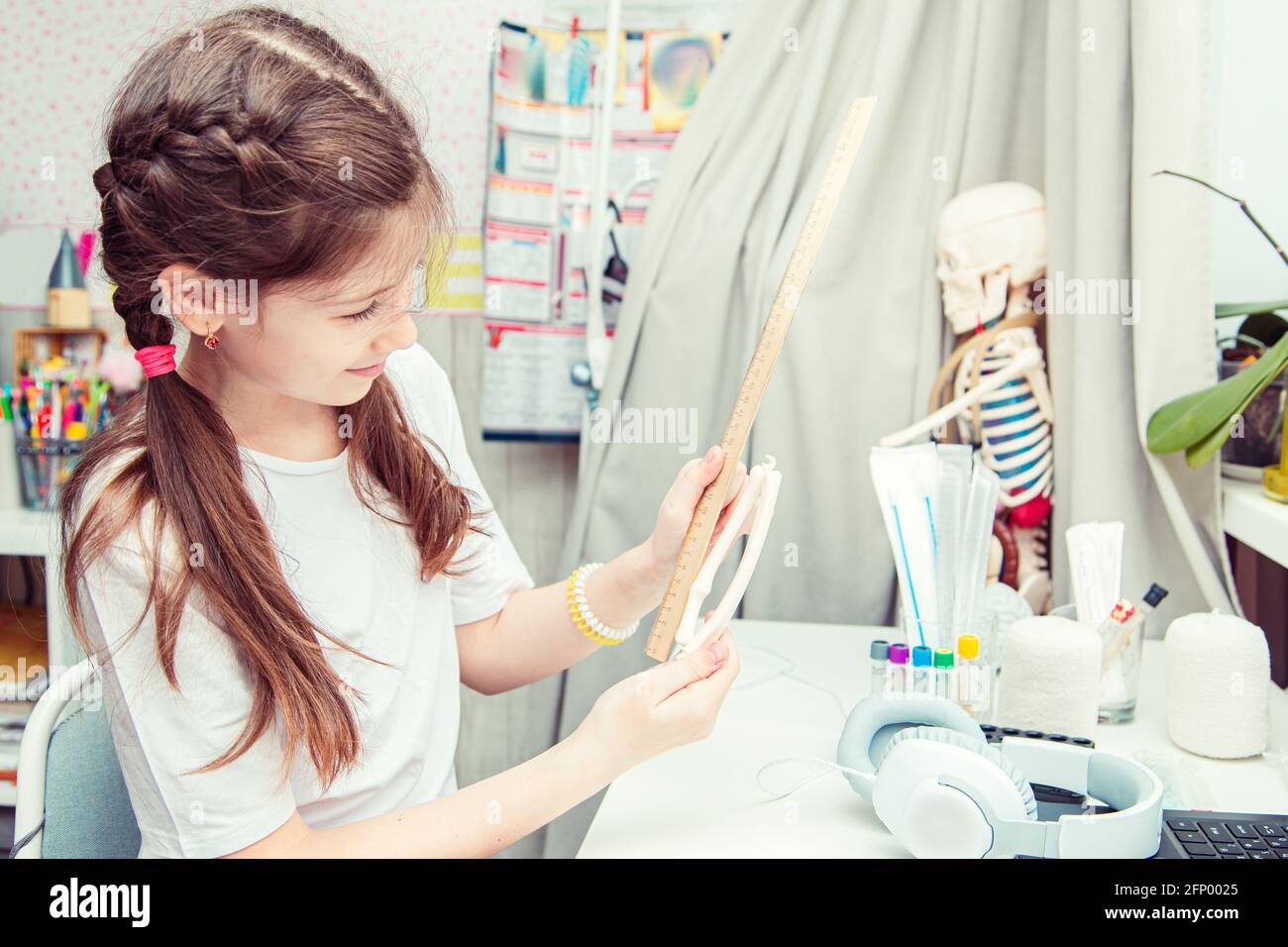 Junges Teenager-Mädchen, das zu Hause menschliche Anatomie studiert. Sie misst den Knochen des ...