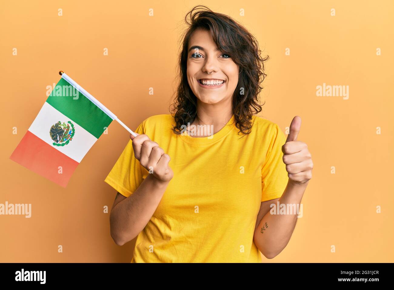 Junge hispanische Frau, die die mexikanische Flagge hält, lächelt glücklich und positiv, tut mit ...