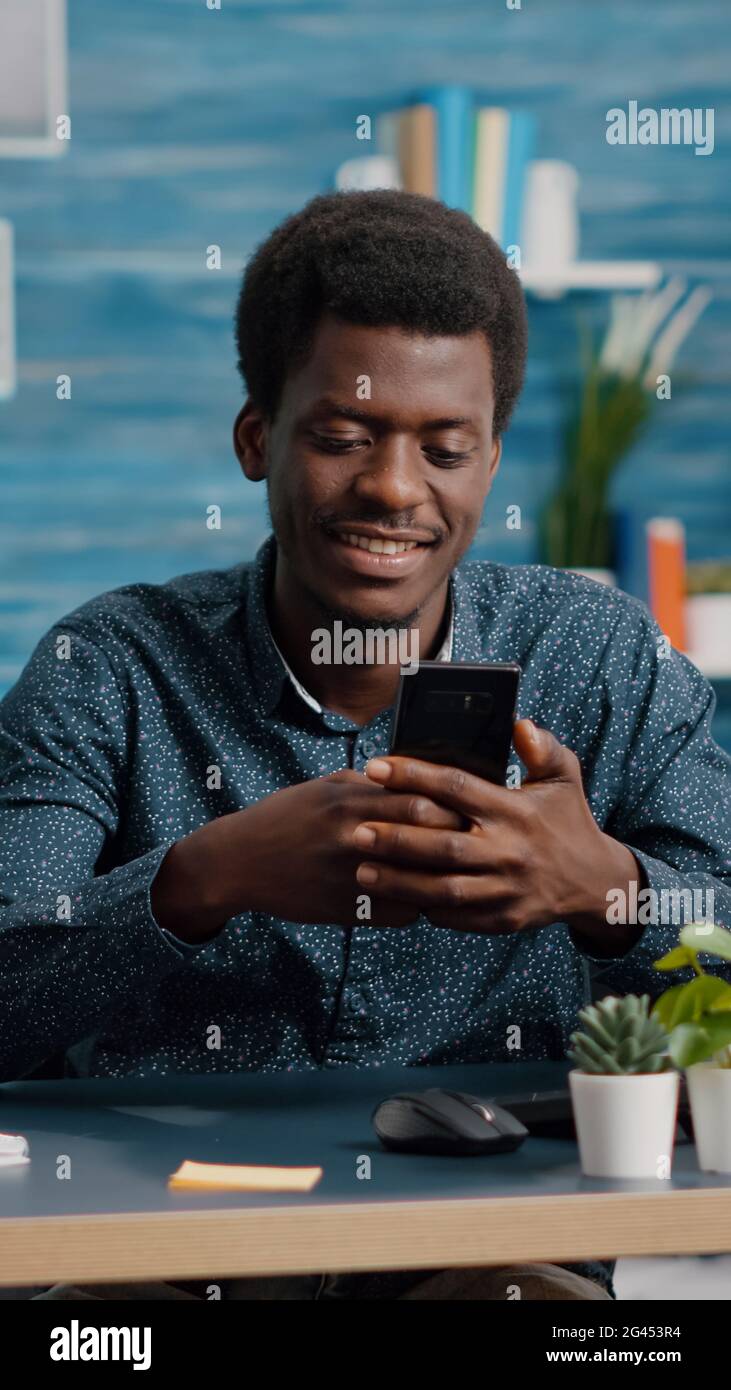 Schwarzer Mann im Wohnzimmer, der Social-Media-Inhalte am Telefon ...