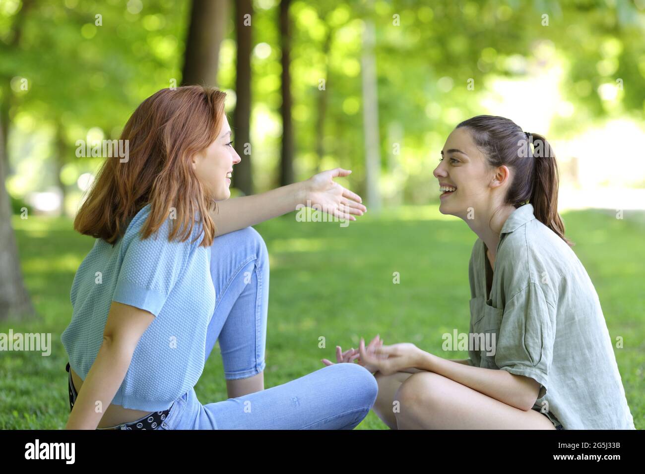 Zwei glückliche Freunde, die im Park auf dem Rasen sitzen und sich ...