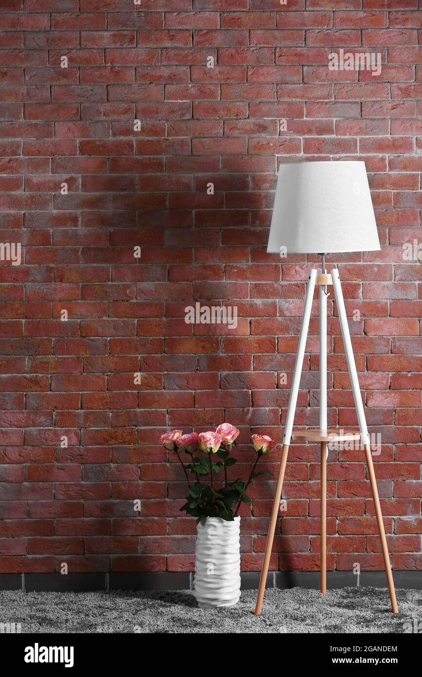 Weißer moderner Stuhl mit Lampe und Strauß Rosen auf Backstein Wand ...