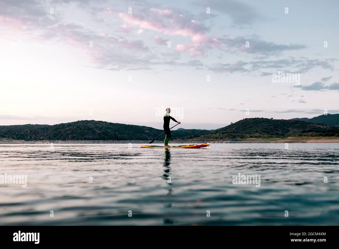 Seitenansicht des anonymen männlichen Surfers, der im Sommer bei Sonnenuntergang auf dem SUP ...