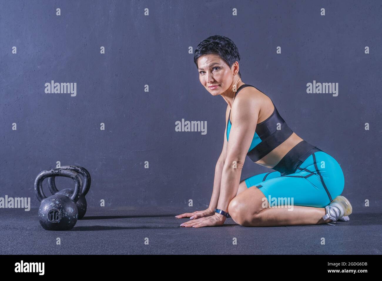 Eine junge Frau in einem Trainingsanzug sitzt auf ihren Knien auf dem ...