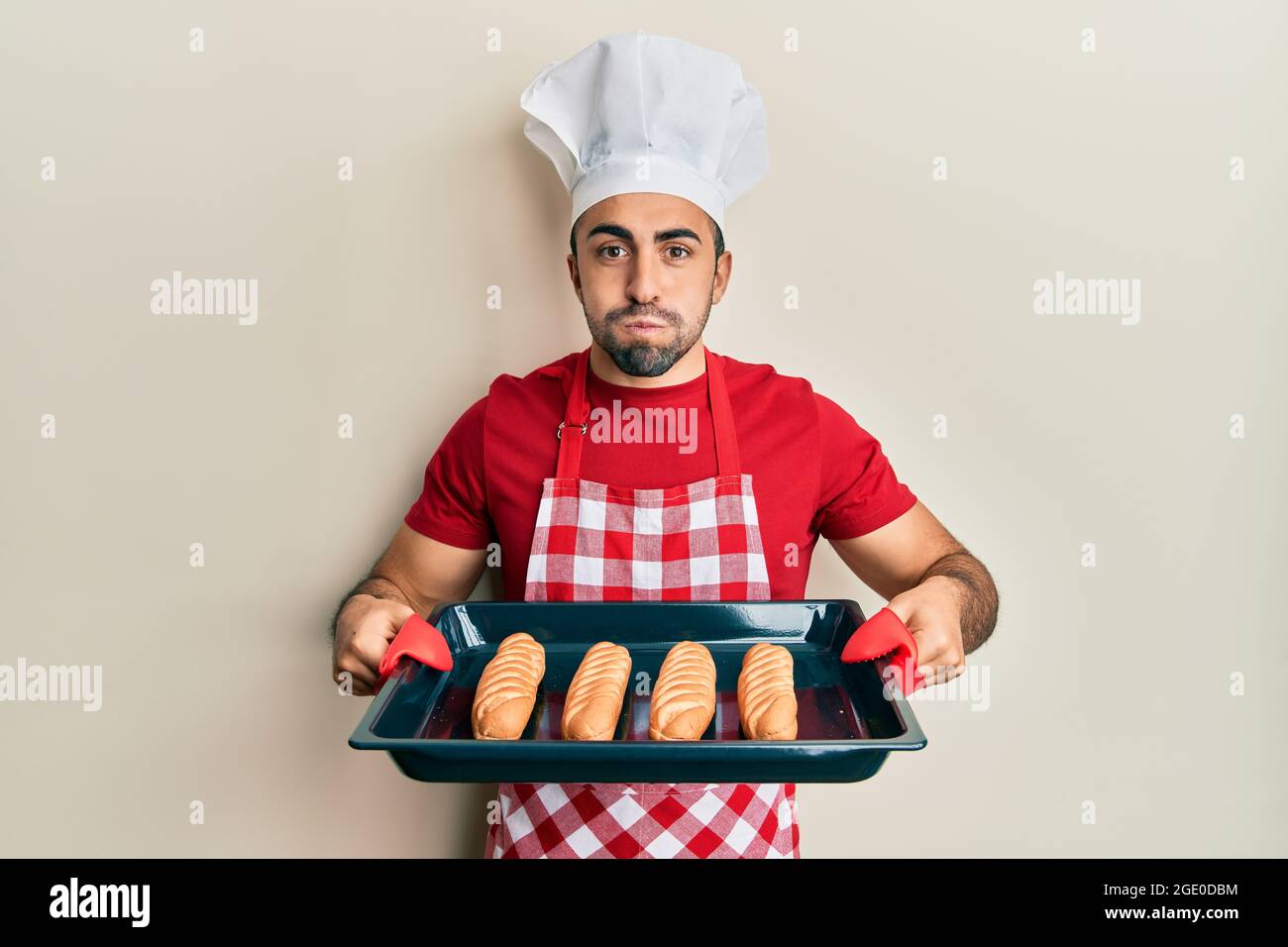 Junger hispanischer Mann trägt Bäckeruniform und hält selbstgebackenes ...