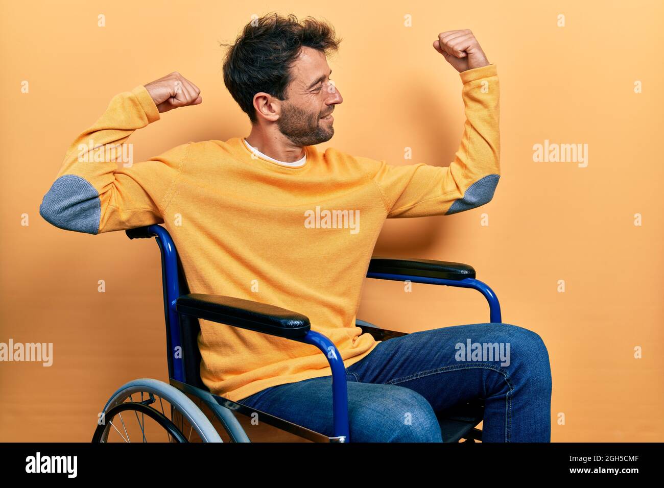 Hübscher Mann mit Bart auf dem Rollstuhl sitzend, zeigt Arme, die Muskeln lächeln stolz ...