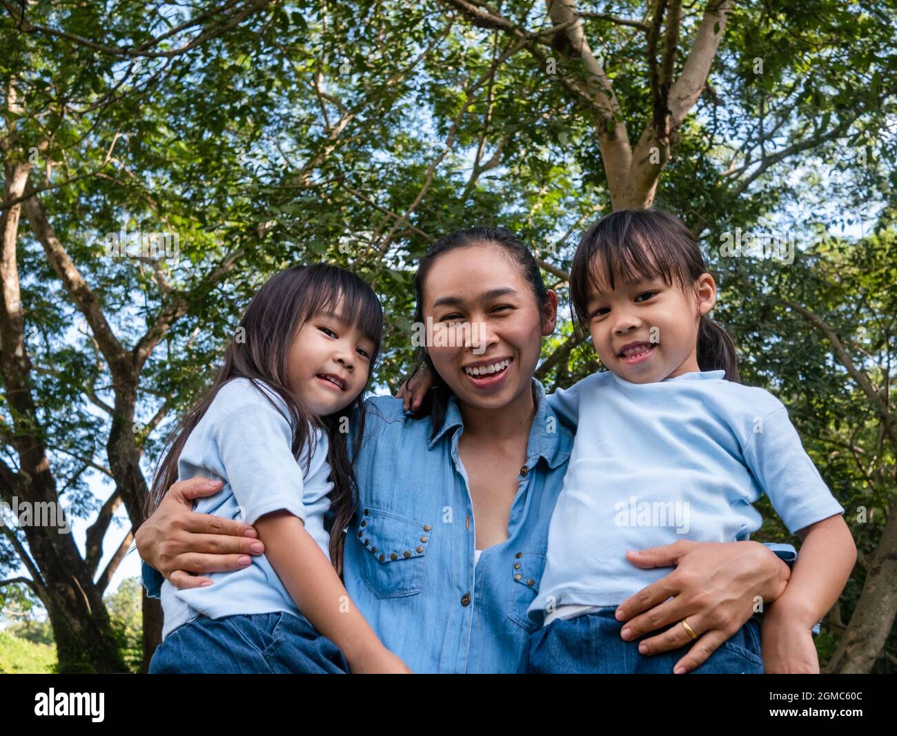 Zwei Geschwistermädchen mit Mama lachen und umarmen sich an warmen und ...