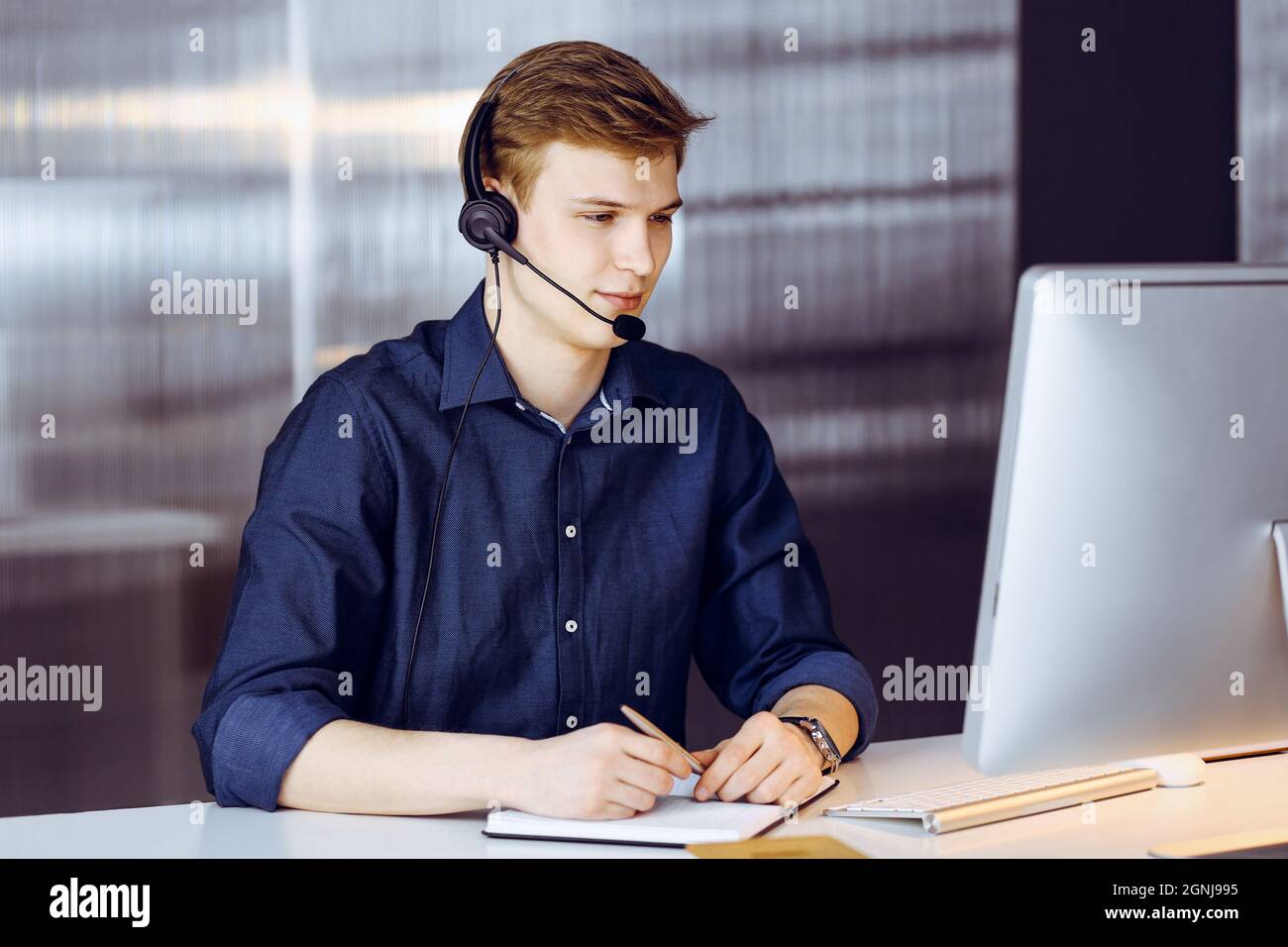 Junge blonde Geschäftsmann mit Headset und Computer bei der Arbeit ...