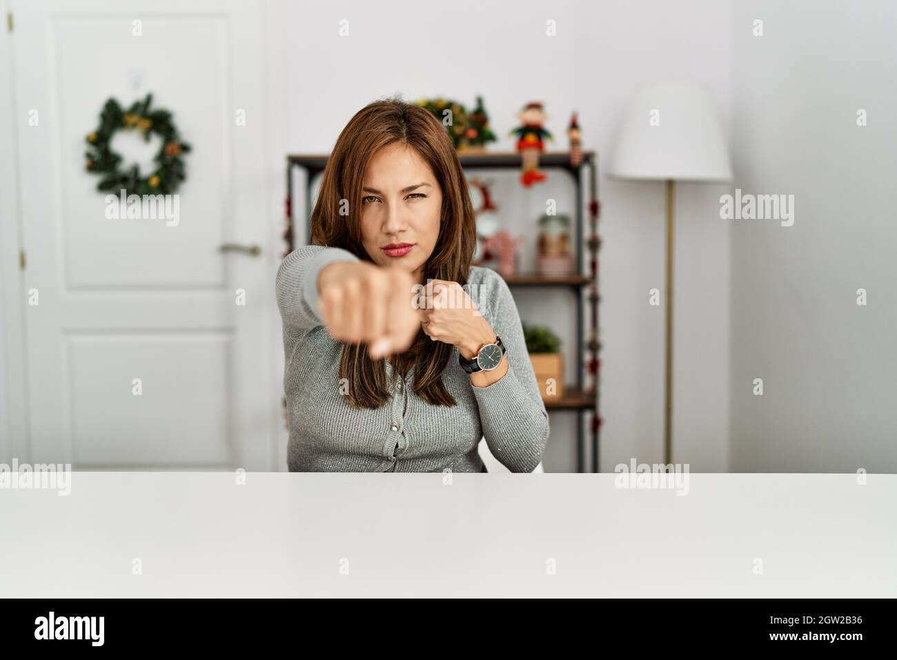 Junge latinerin sitzt auf dem Tisch bei weihnachtsdekor stampfen Faust zu kämpfen, aggressive ...