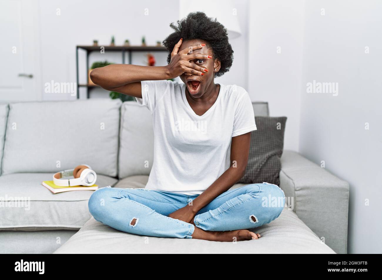 Afrikanische junge Frau, die zu Hause auf dem Sofa sitzt und mit der ...