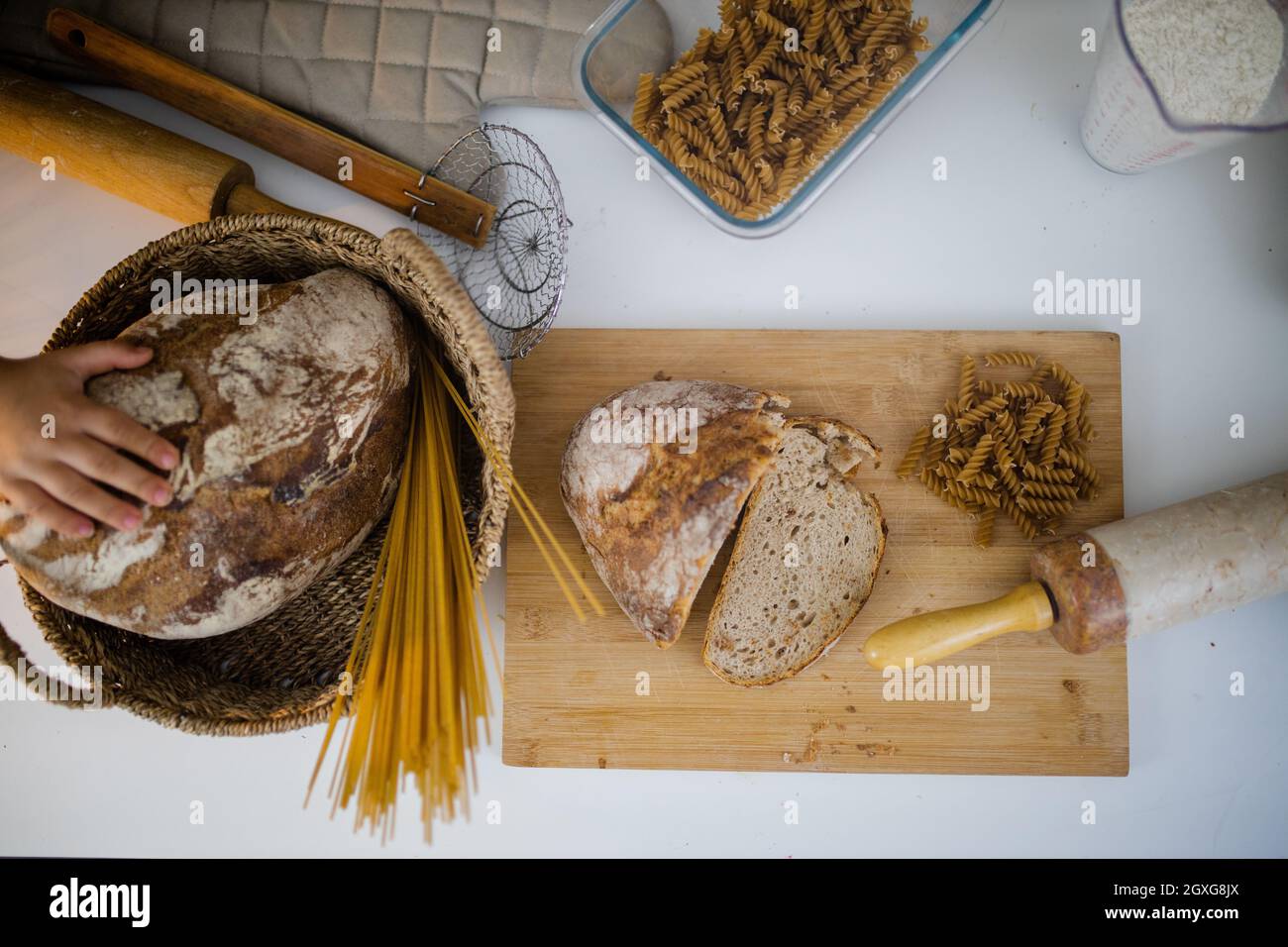 Brot, Nudeln, Mehl und Kochgeschirr aus Holz auf weißem Tisch von oben ...