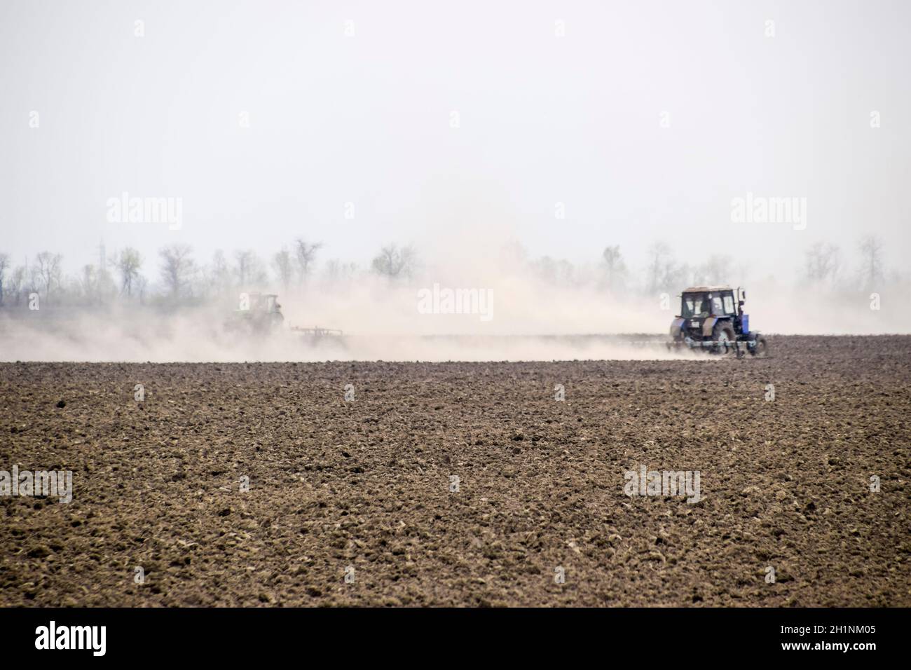 Der Traktor Eggen der Boden, auf dem Feld und schafft eine Staubwolke ...