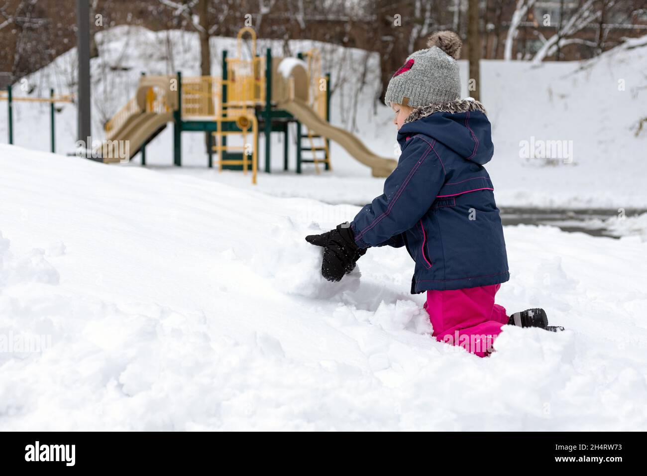 Kleines Kind, das im Winter auf dem Spielplatz mit Schnee spielt ...