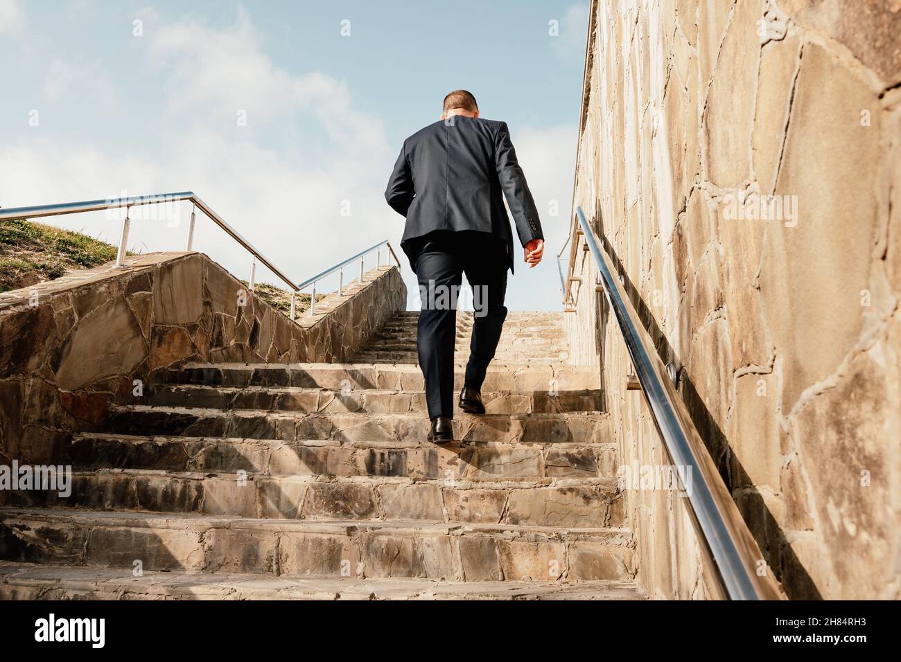 Selbstbewusster Geschäftsmann mittleren Alters mit Aktentasche, der die Treppe hoch läuft ...