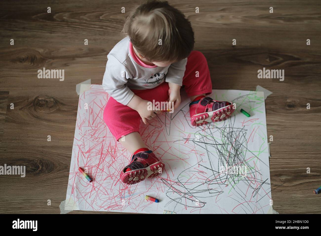 Das kleine Mädchen zeichnet mit Buntstiften auf ein großes weißes Blatt ...