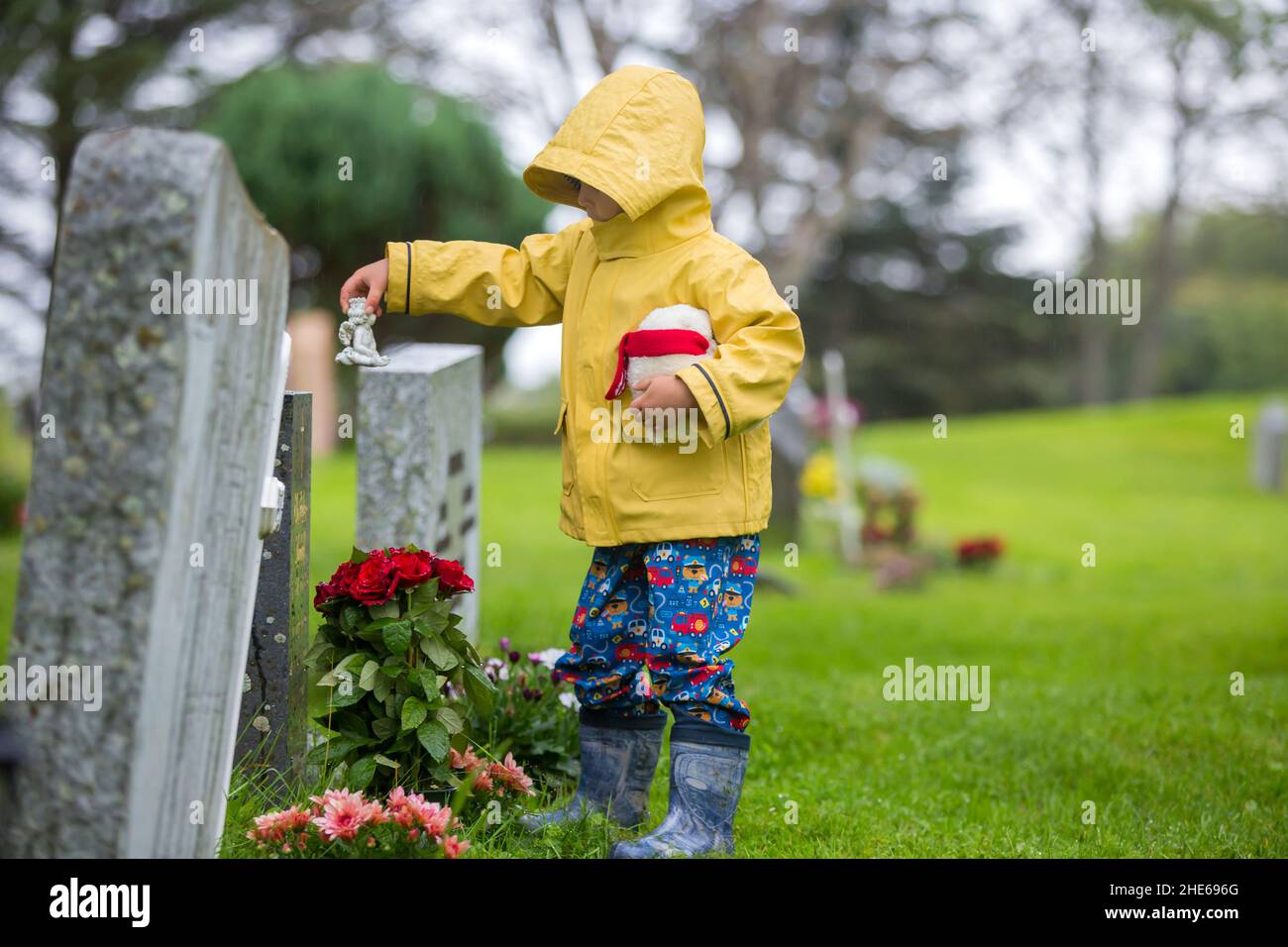 Trauriges kleines Kind, blonder Junge, im Regen auf dem Friedhof stehend, traurige Person ...