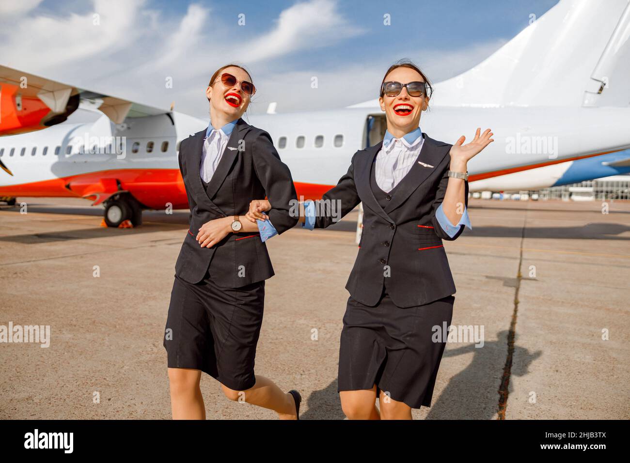 Lächelnde Flugbegleiterinnen, die am Flughafen Arm in Arm gehen ...