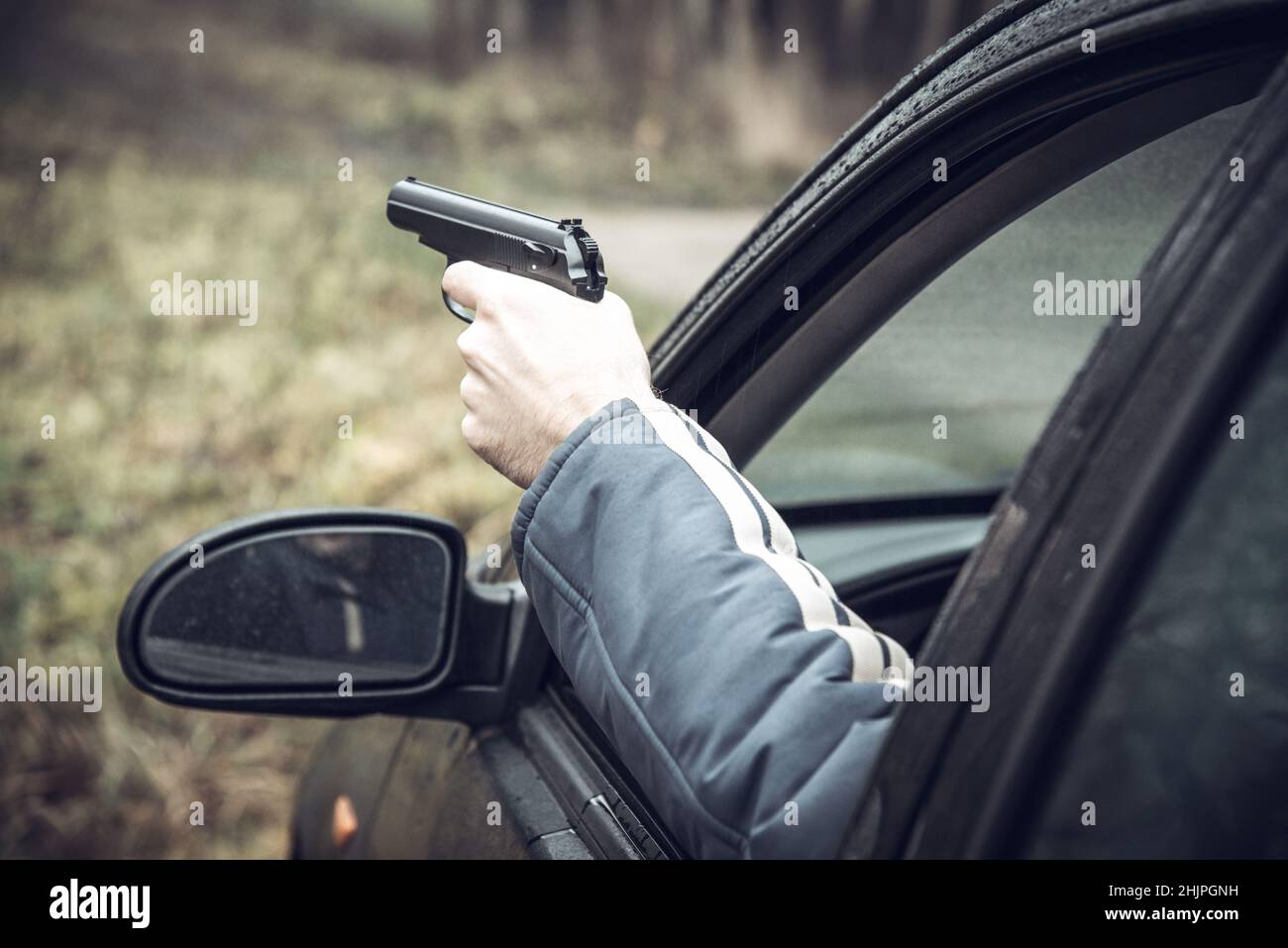 Ein Mann mit einer Waffe, der ein Auto fährt, die Hand eines Mannes mit ...