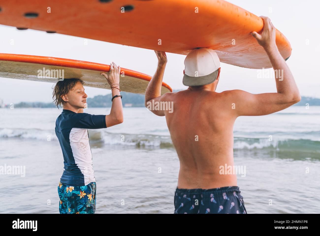Teenager-Junge mit seinem Vater mit Surfbrettern auf den Köpfen, die in ... Teenager-Junge mit seinem Vater mit Surfbrettern auf den Köpfen, die in ...