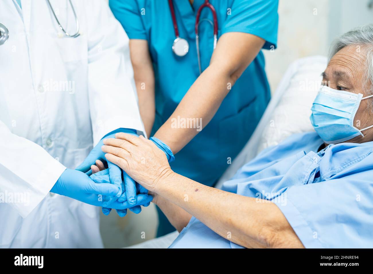 Das asiatische Ärzteteam und die alte ältere Dame-Patientin stapeln sich als Team zusammen, um ...