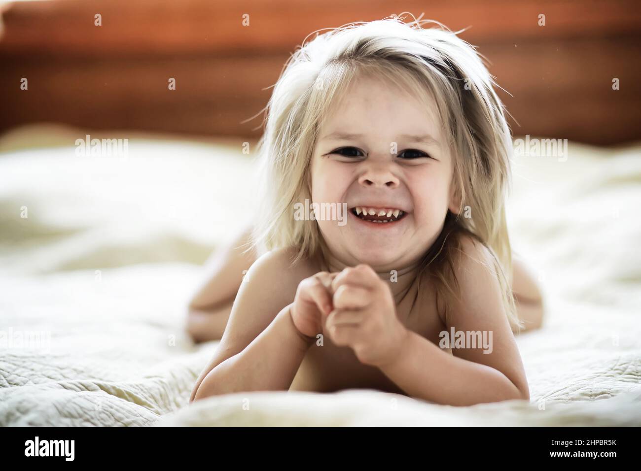 Kleines blondes Mädchen liegt auf dem Bett. Emotionales Kind Kind Kind posiert Stockfotografie ...
