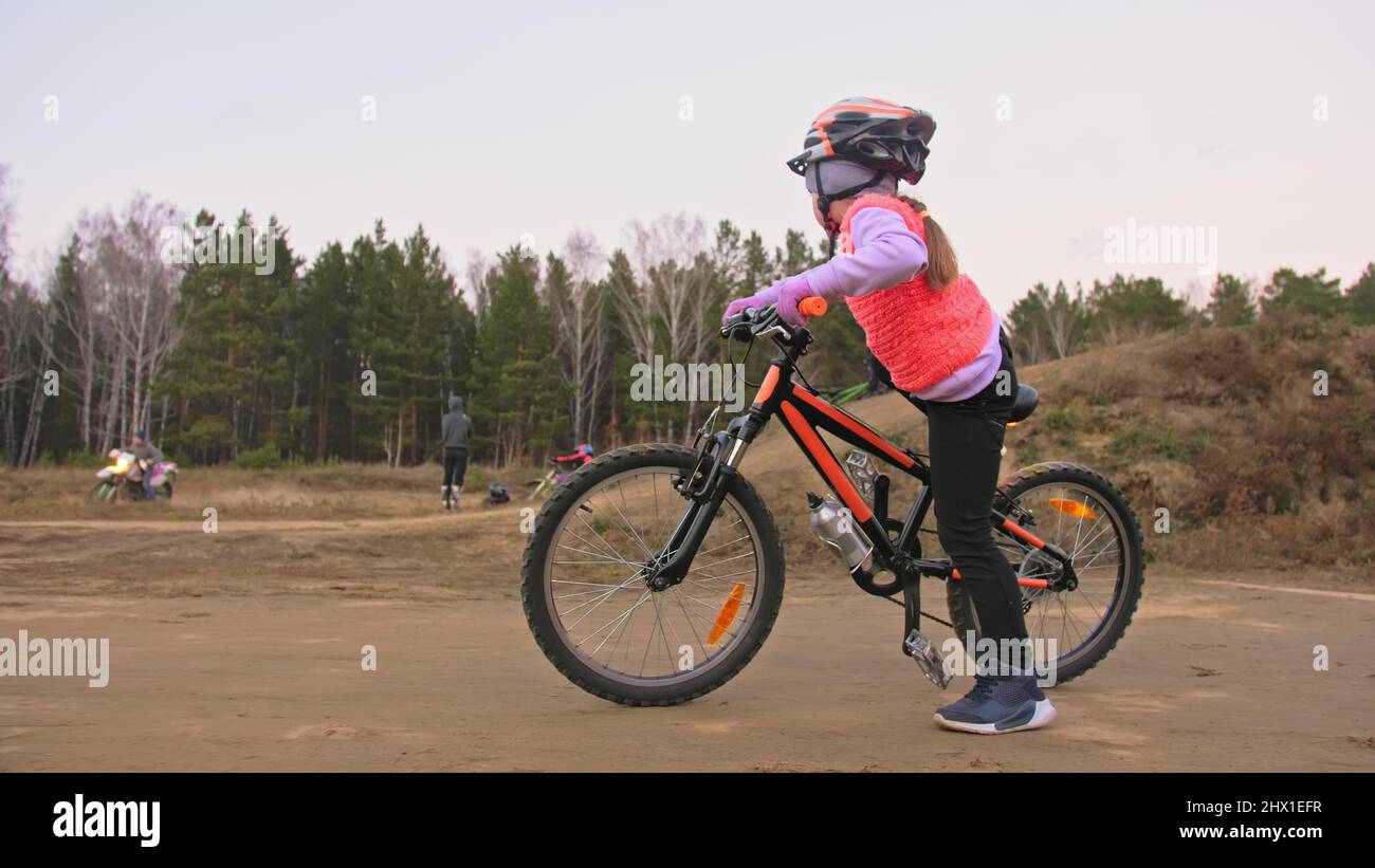 Ein kaukasisches Kind fährt auf einer Fahrradstraße im Schotterpark. Mädchen reiten schwarz ...