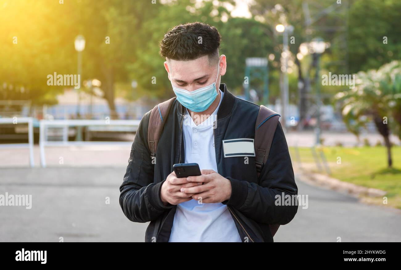 Hübscher Kerl, der mit seinem Telefon schreibt, hübscher junger Mann in Gesichtsmaske, der mit ...