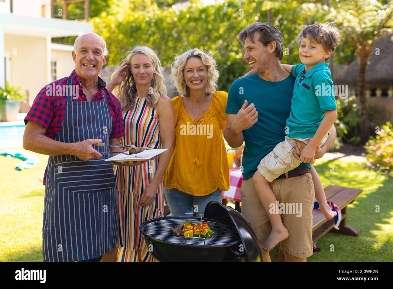 Portrait einer lächelnden kaukasischen Familie aus drei Generationen, die im Garten grillen ...