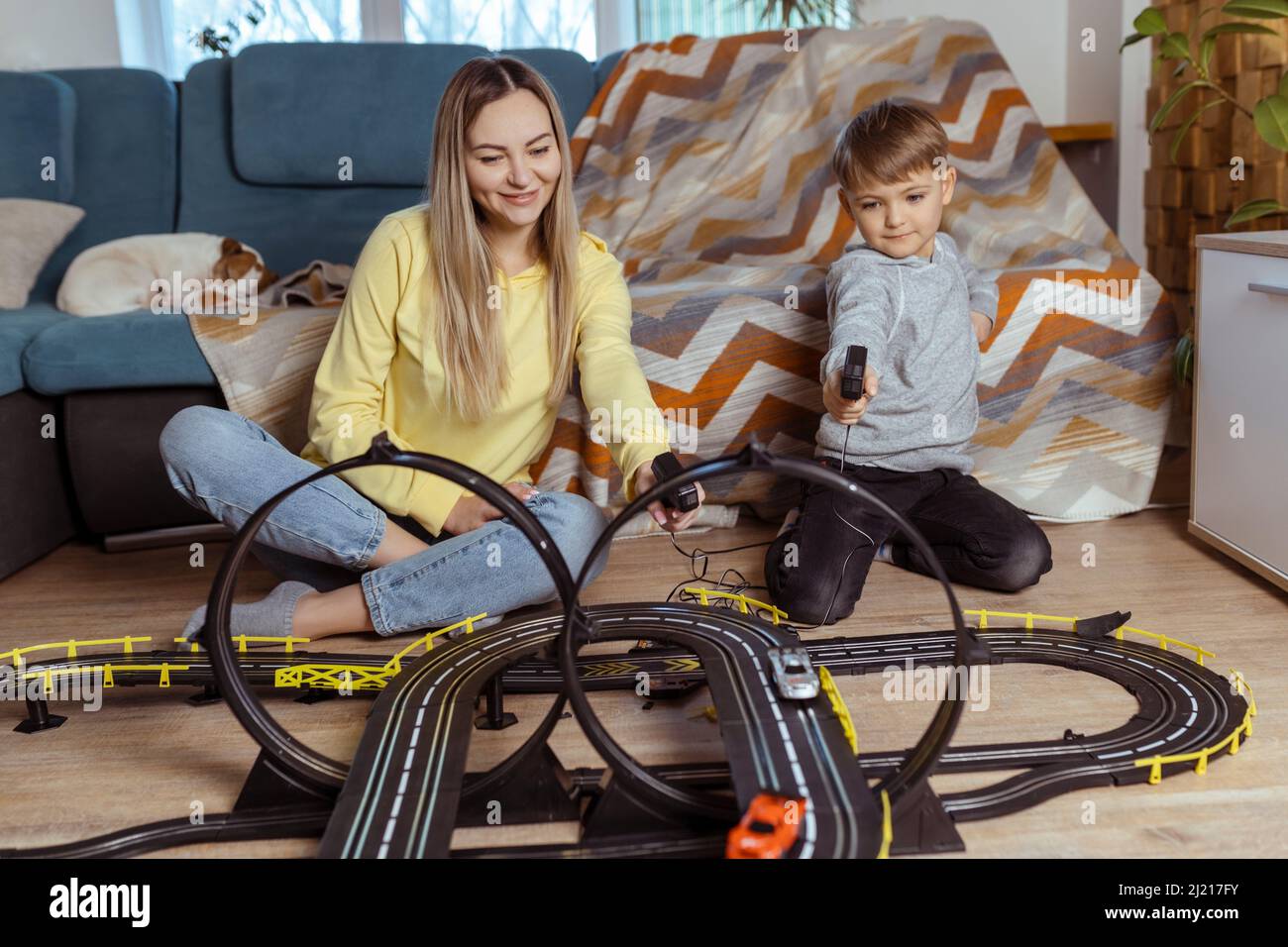 Mama und kleiner Sohn spielen zu Hause auf dem Teppich Rennen, haben ...