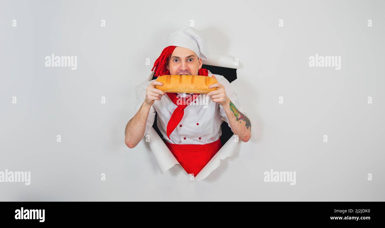 Junger Mann mit roten Dreadlocks, der als Koch weißes Brot beißt, steht ...